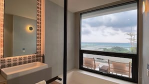 Um banheiro com uma janela grande, uma banheira e um espelho com aplicação de azulejos geométricos.