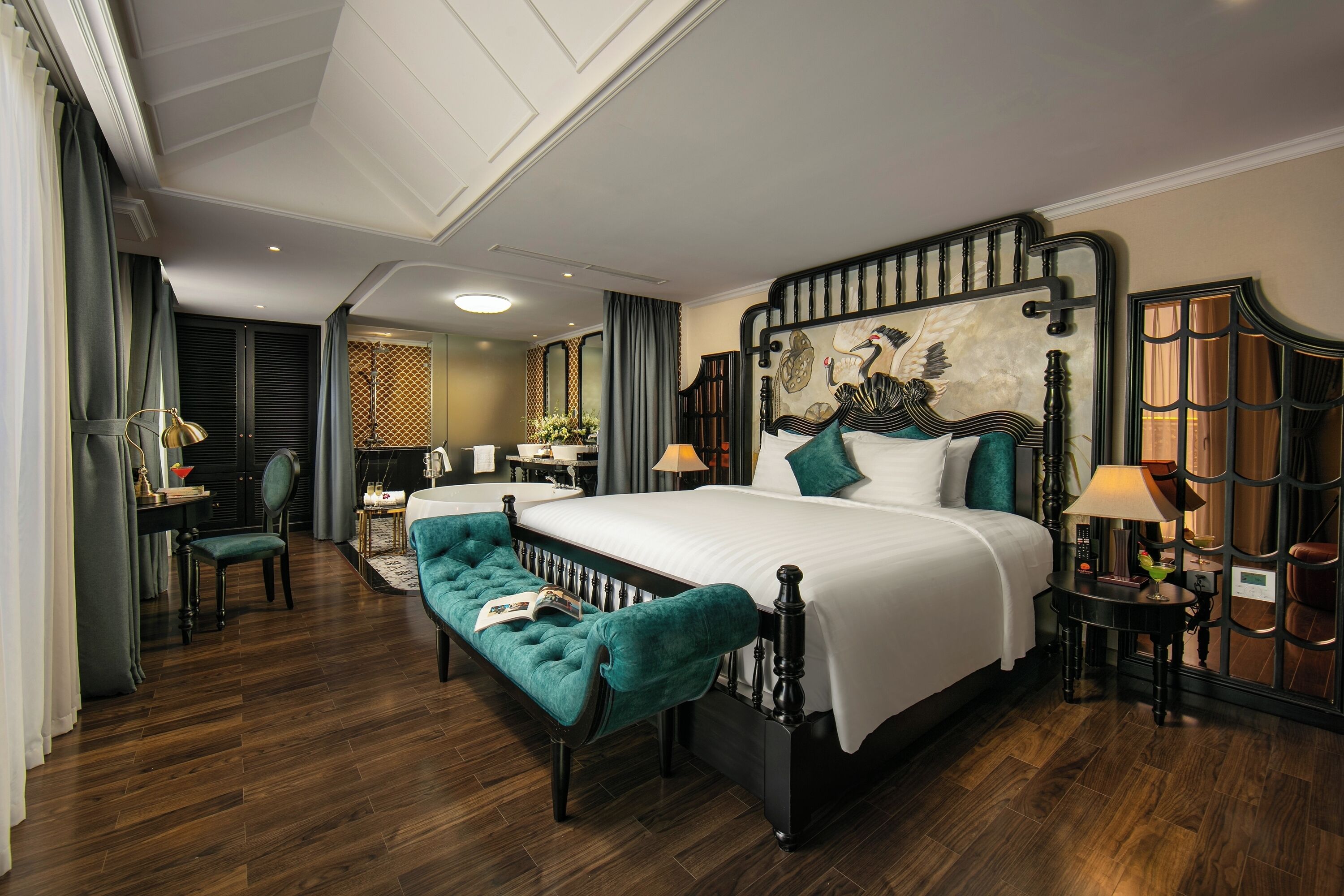 Quarto de hotel com uma cama grande, um banco, uma escrivaninha e uma cadeira.