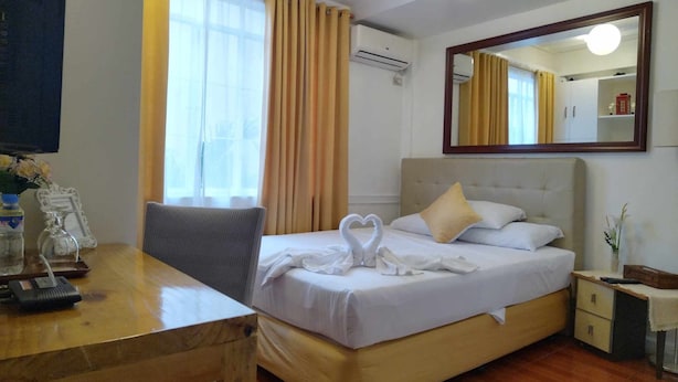 Quarto de hotel com cama, mesa de cabeceira, cadeira e escrivaninha com espelho.