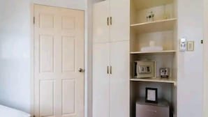 Quarto com porta branca, guarda-roupa branco e uma pequena geladeira.