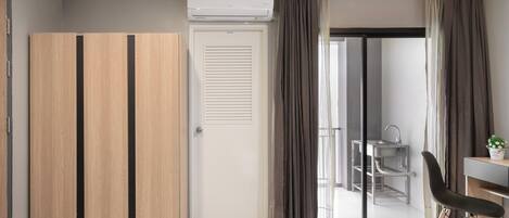 Quarto de hotel moderno com guarda-roupa de madeira, cama com manta verde, escrivaninha com cadeira e vista para uma varanda com pia.
