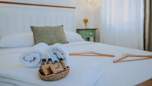 Cama bem arrumada com toalhas brancas dobradas, um cesto de amenities e cabides de madeira em uma cama de quarto de hotel.