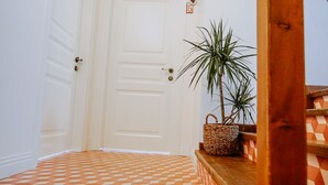 Um corredor com piso xadrez, uma porta branca e escada de madeira.