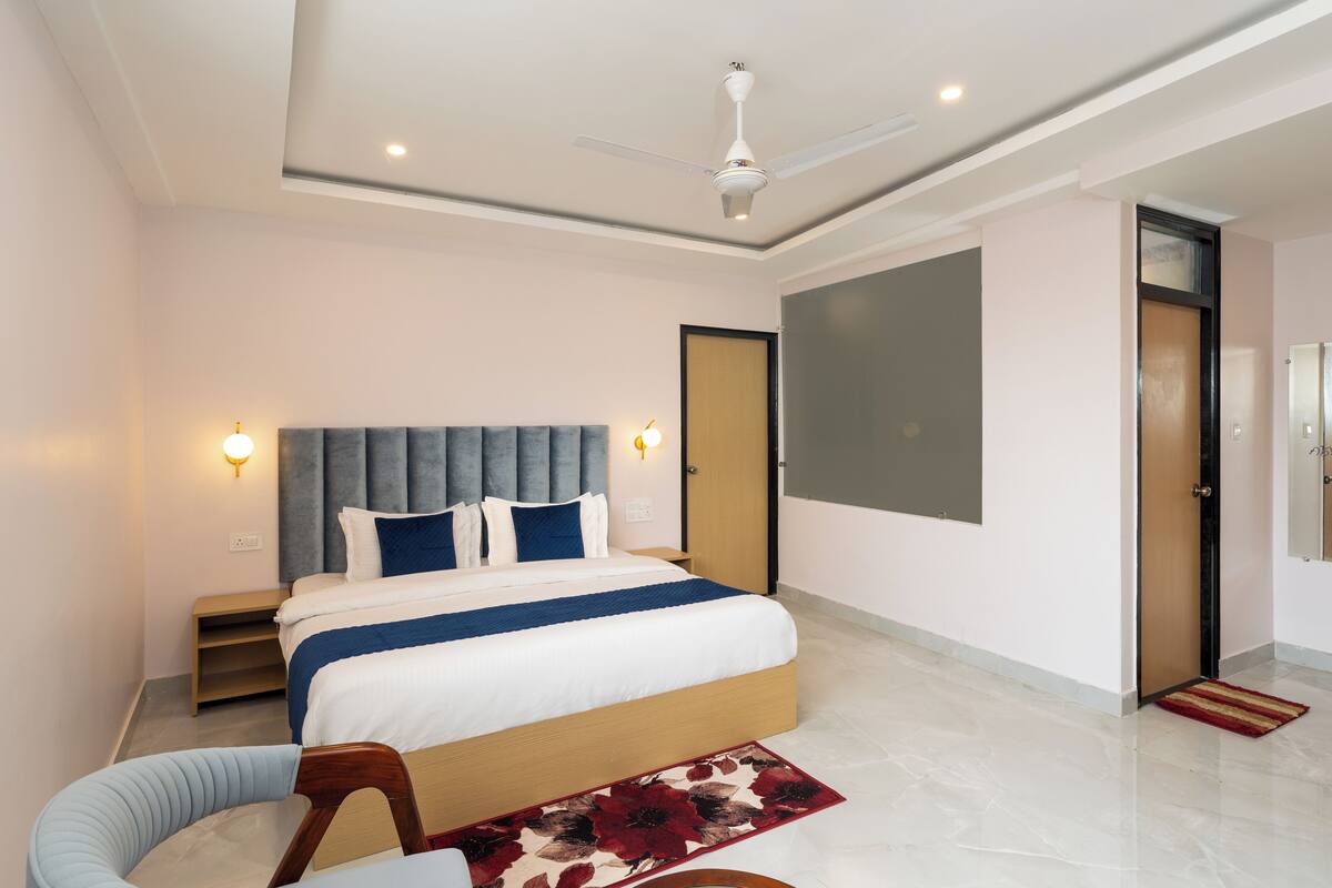 Quarto de hotel moderno com uma cama grande, um ventilador de teto, uma mesinha de cabeceira e uma TV fixada na parede.