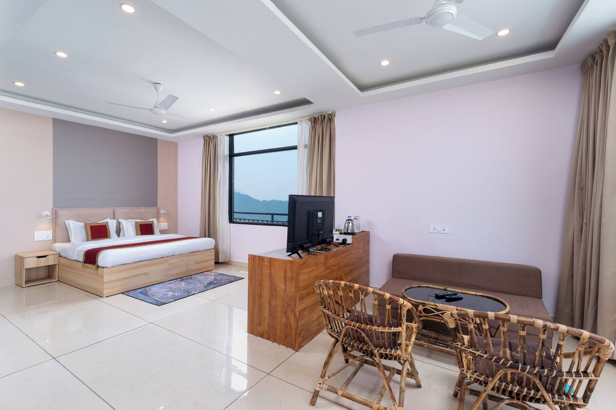 Quarto de hotel com cama, escrivaninha com televisão, sofá e mesa de jantar com cadeiras.