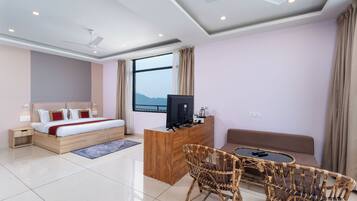 Quarto de hotel com cama, escrivaninha com televisão, sofá e mesa de jantar com cadeiras.