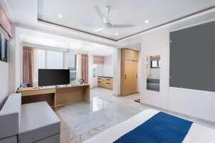 Quarto de hotel moderno com uma cama grande, escrivaninha, televisão de tela plana, guarda-roupa e banheiro.