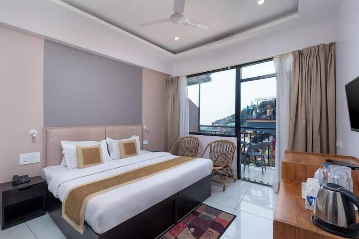 Quarto de hotel com cama, escrivaninha com chaleira, uma cadeira e uma televisão.