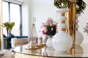 Uma sala de estar moderna com uma mesa de centro de vidro, vasos brancos e dourados, e uma planta decorativa.