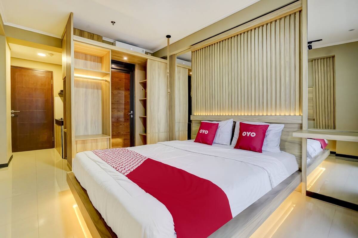 Quarto de hotel moderno com cama grande, cabeceira de madeira e estantes embutidas.