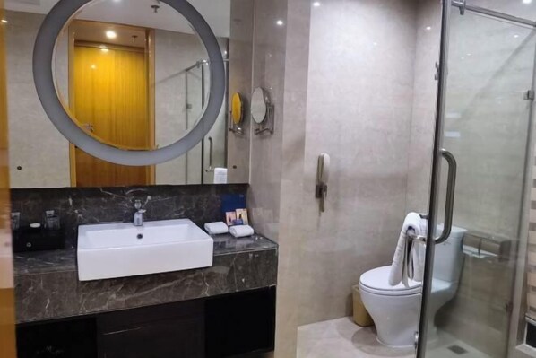 Uma casa de banho moderna com uma pia de mármore, chuveiro com divisória de vidro e porta de madeira ao fundo.