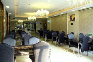 Espaço de refeições de hotel com várias mesas e cadeiras, lustres e um espelho refletindo o ambiente.