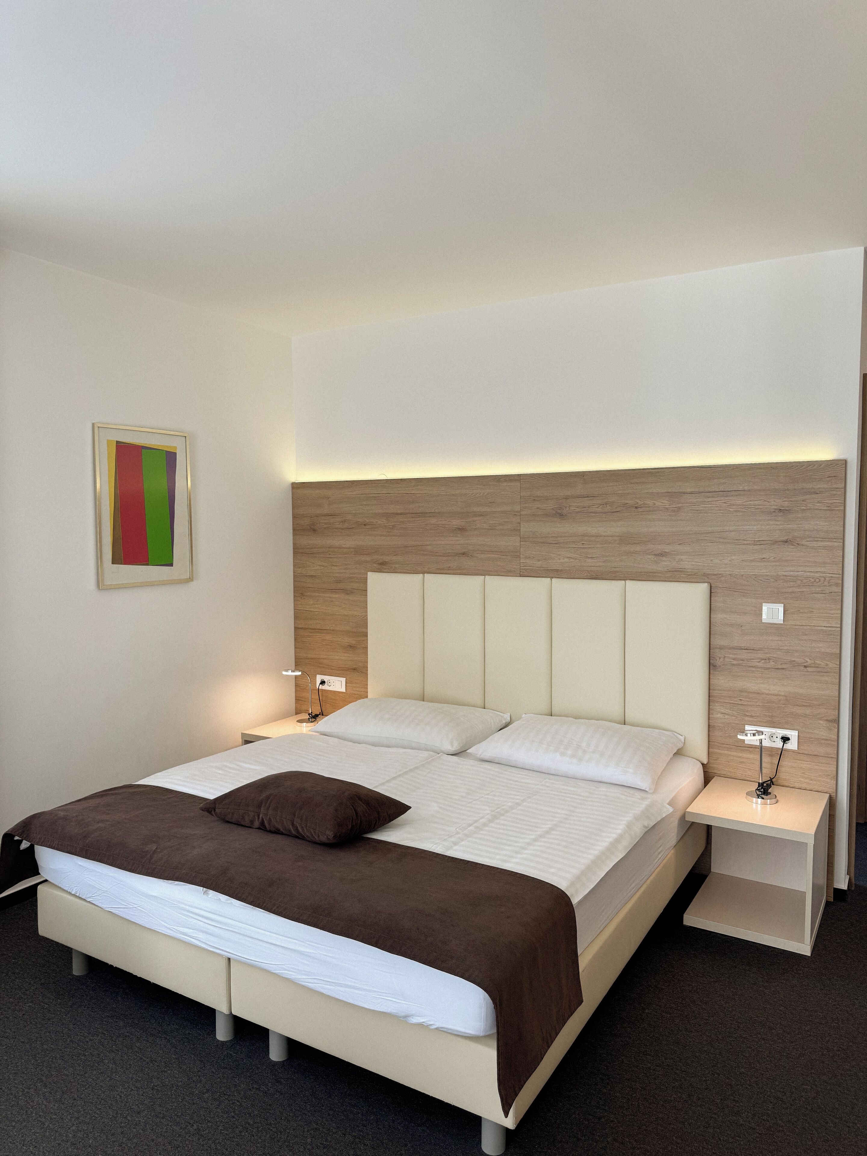 Quarto de hotel moderno com cama grande, mesas de cabeceira e uma obra de arte na parede.