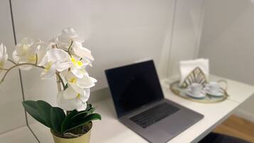 Uma mesa com um laptop, uma orquídea em vaso e um objeto decorativo com xícaras e pireses.