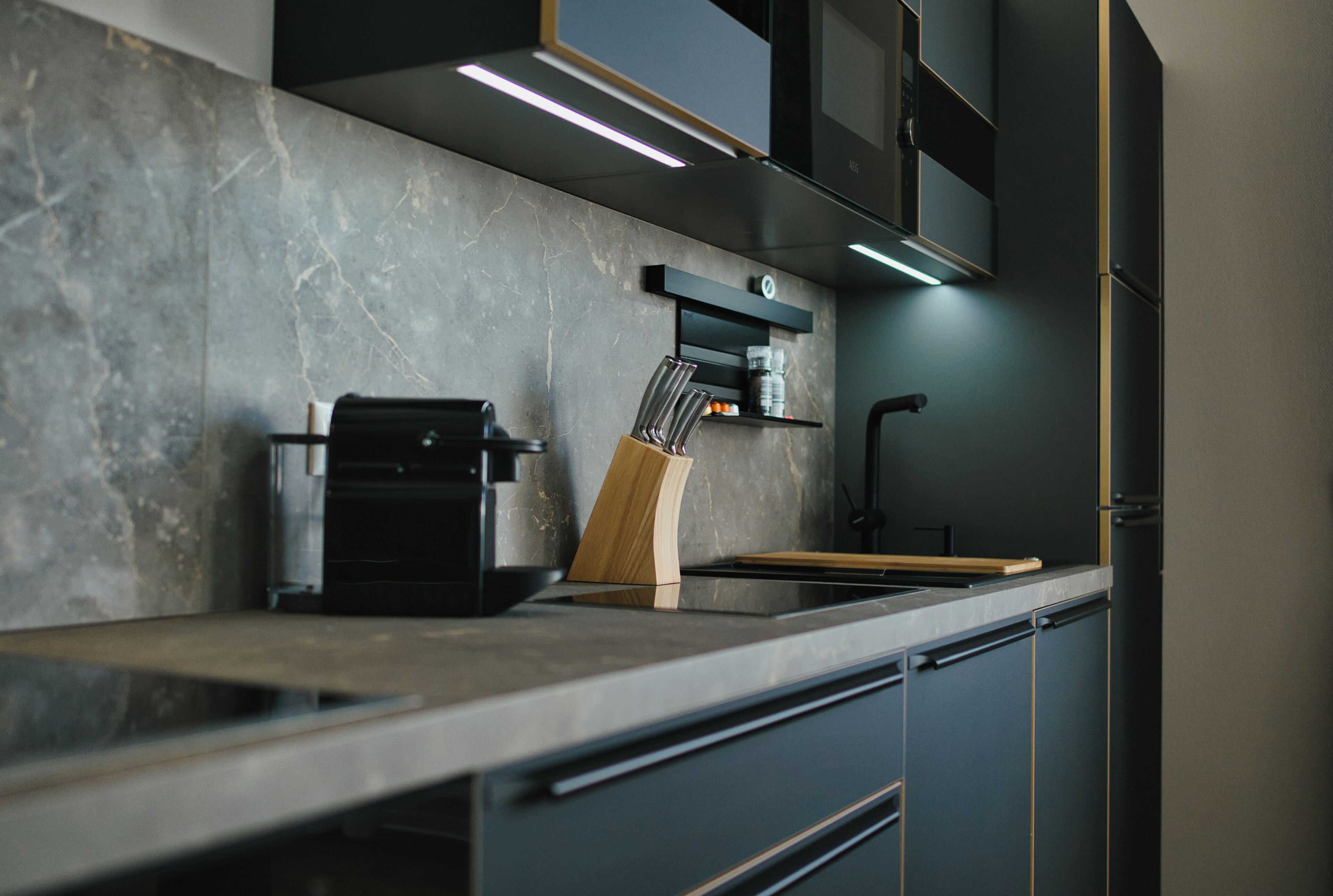 Uma cozinha moderna com forno embutido, máquina de café e suporte para facas na bancada.