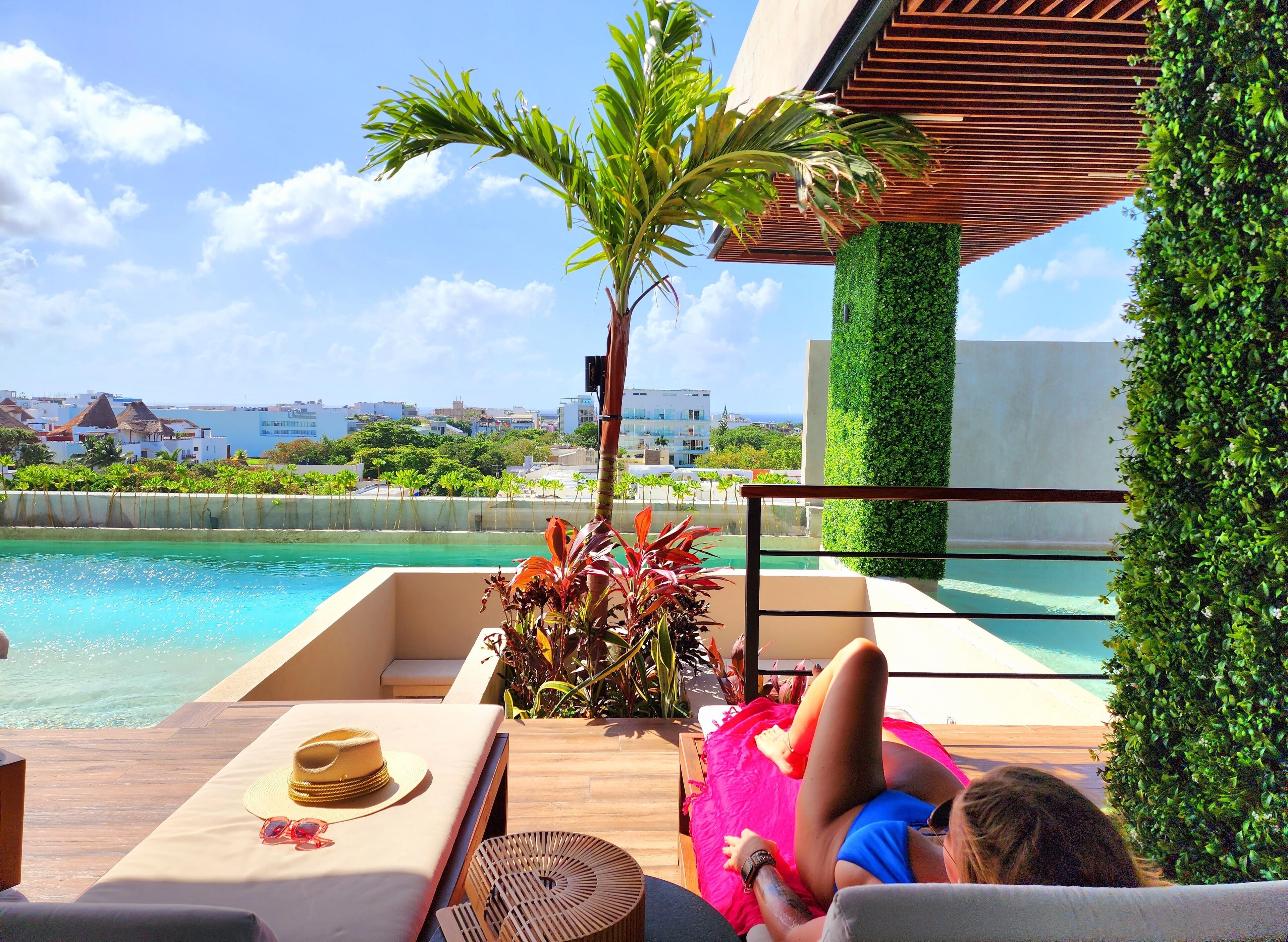 Uma área de descanso à beira da piscina, com vista para o oceano, uma palmeira e um jardim vertical verde.
