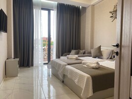 Quarto de hotel com duas camas, televisão e varanda com cortinas.