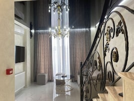 Uma sala de estar moderna com um candelabro, uma mesa redonda e uma escada com grades de metal elaboradas.