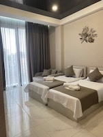 Quarto de hotel moderno com duas camas, uma janela grande com cortinas e um detalhe decorativo na parede.