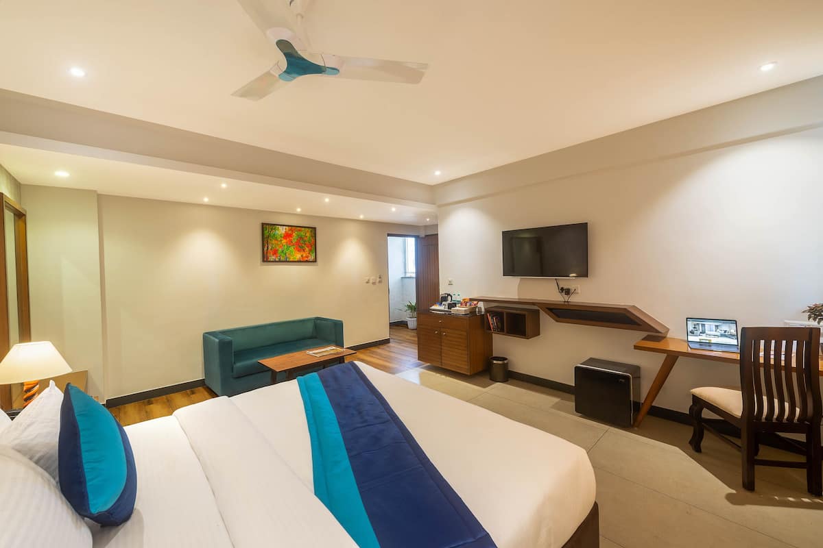 Quarto de hotel com cama, escrivaninha, cadeira, televisão e ventoinha no teto.