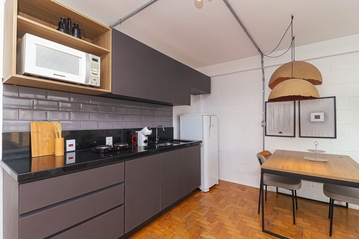 Cozinha moderna com micro-ondas, fogão e pia. Há uma mesa de jantar de madeira com cadeiras e um refrigerador.