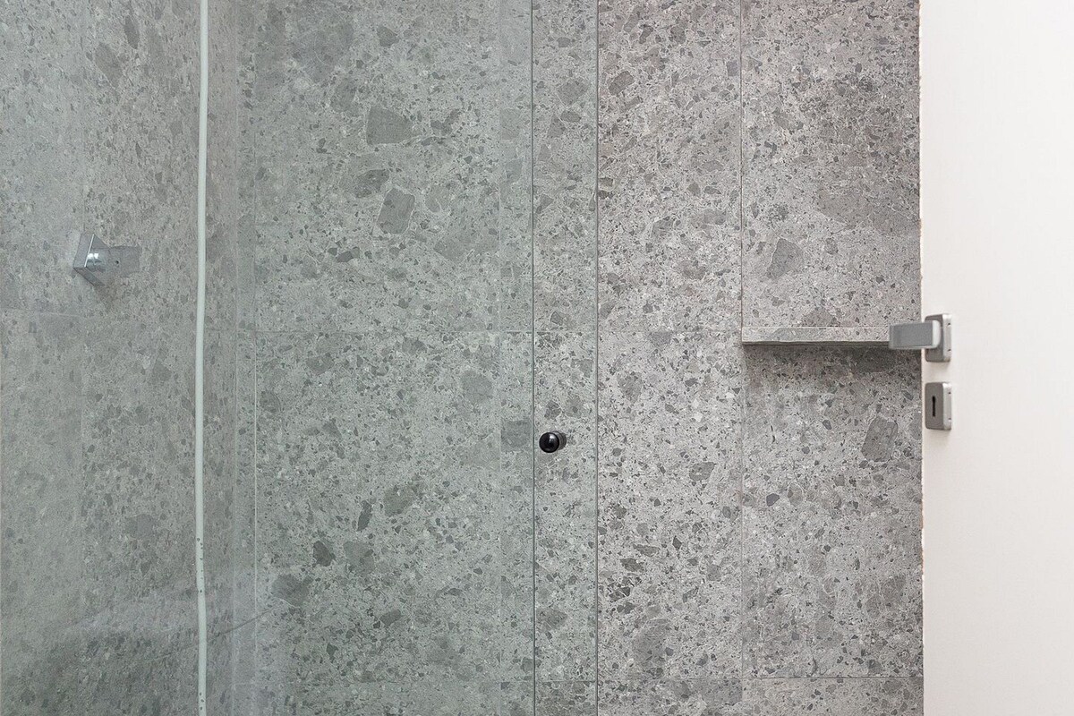 Chuveiro com porta de vidro, chuveiro branco e painel de controle à direita.