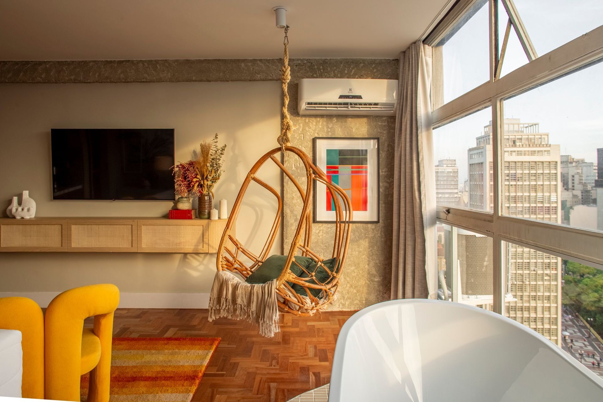 Uma sala de estar moderna com uma janela grande, uma cadeira suspensa, uma TV de tela plana e vista para a cidade.