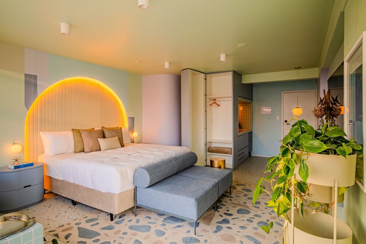 Quarto moderno com cama, mesas de cabeceira, um banco, guarda-roupa e uma planta em vaso.