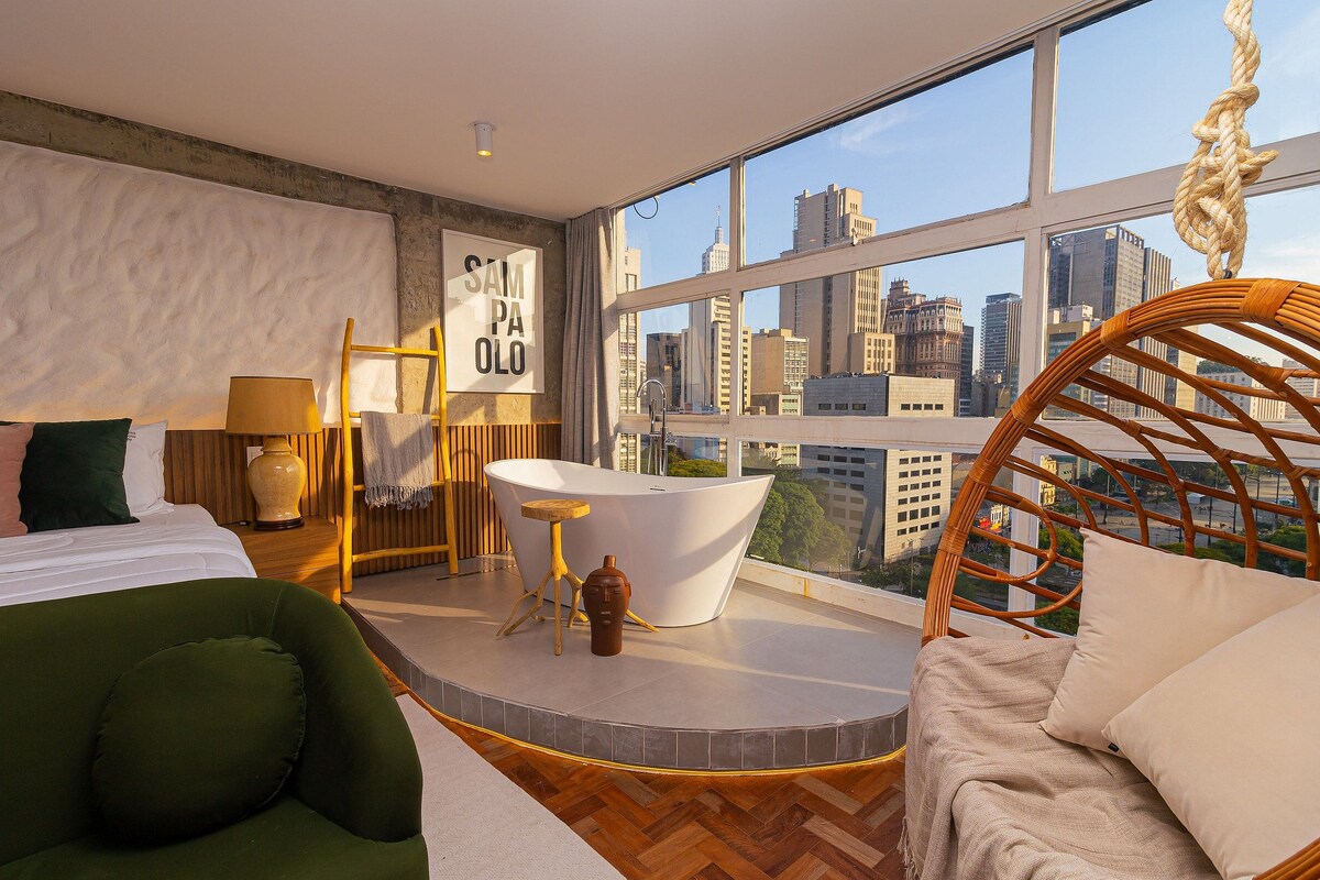 Quarto moderno com vista para a cidade, uma janela grande, uma banheira e um sofá verde.