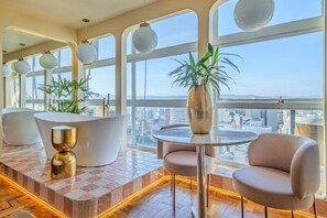 Um interior moderno com uma janela ampla, uma banheira branca, uma mesa redonda e um vaso com planta.