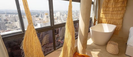 Quarto com uma janela grande, banheira e rede suspensa.