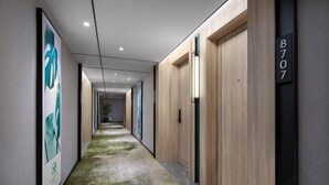 Um corredor com portas de madeira, placa de número e quadros nas paredes.