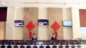 Uma área de recepção com balcão de check-in, dois funcionários e duas televisões na parede.