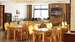 Uma sala de jantar ampla com uma mesa comprida e cadeiras, um lustre, uma televisão na parede e uma grande janela.