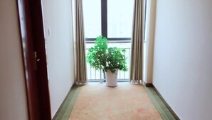 Um corredor com planta em vaso, uma porta e uma janela com cortinas.