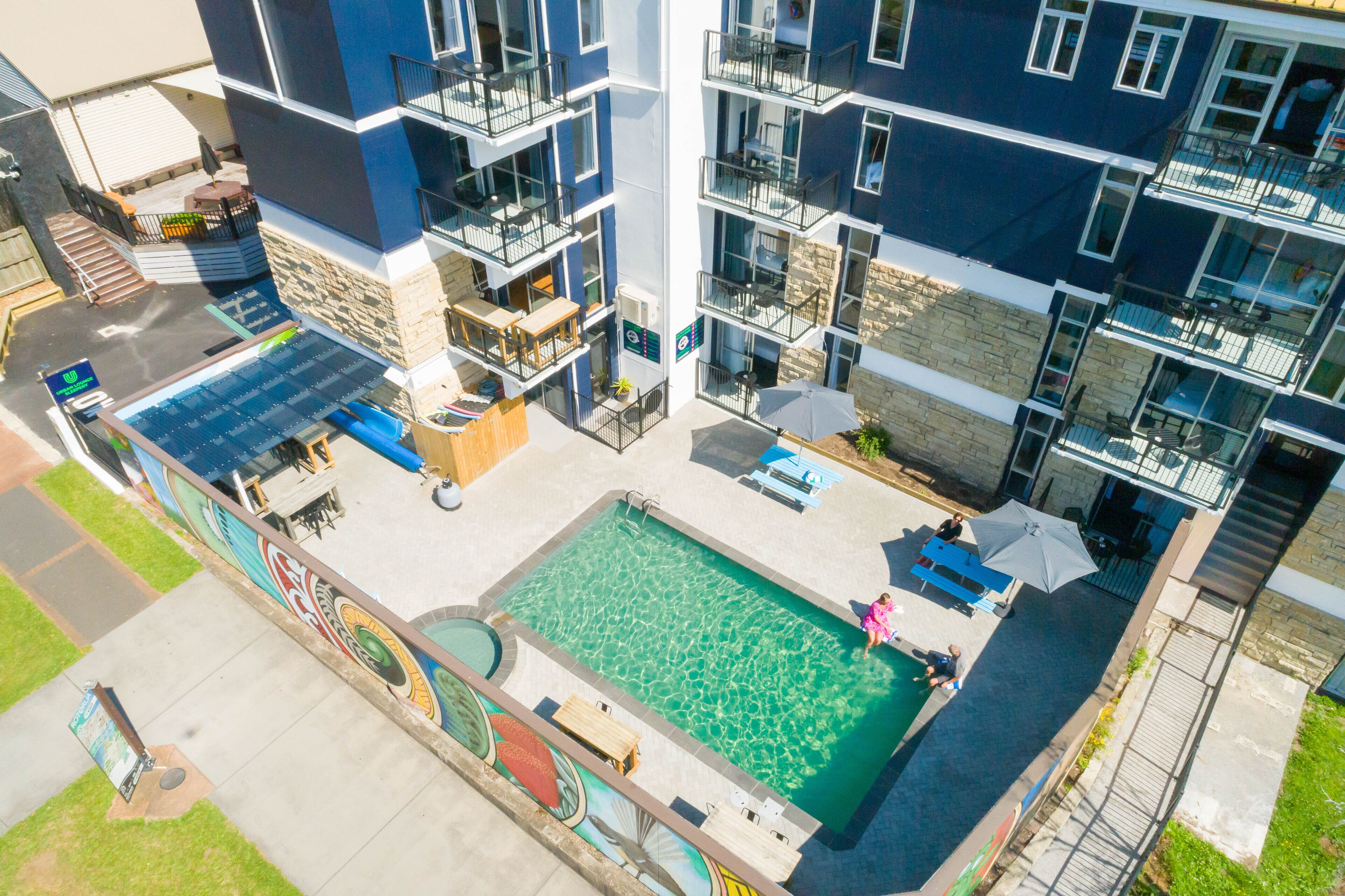 Um edifício de vários andares com área de piscina no terraço, espaço para sentar ao ar livre e um mural.