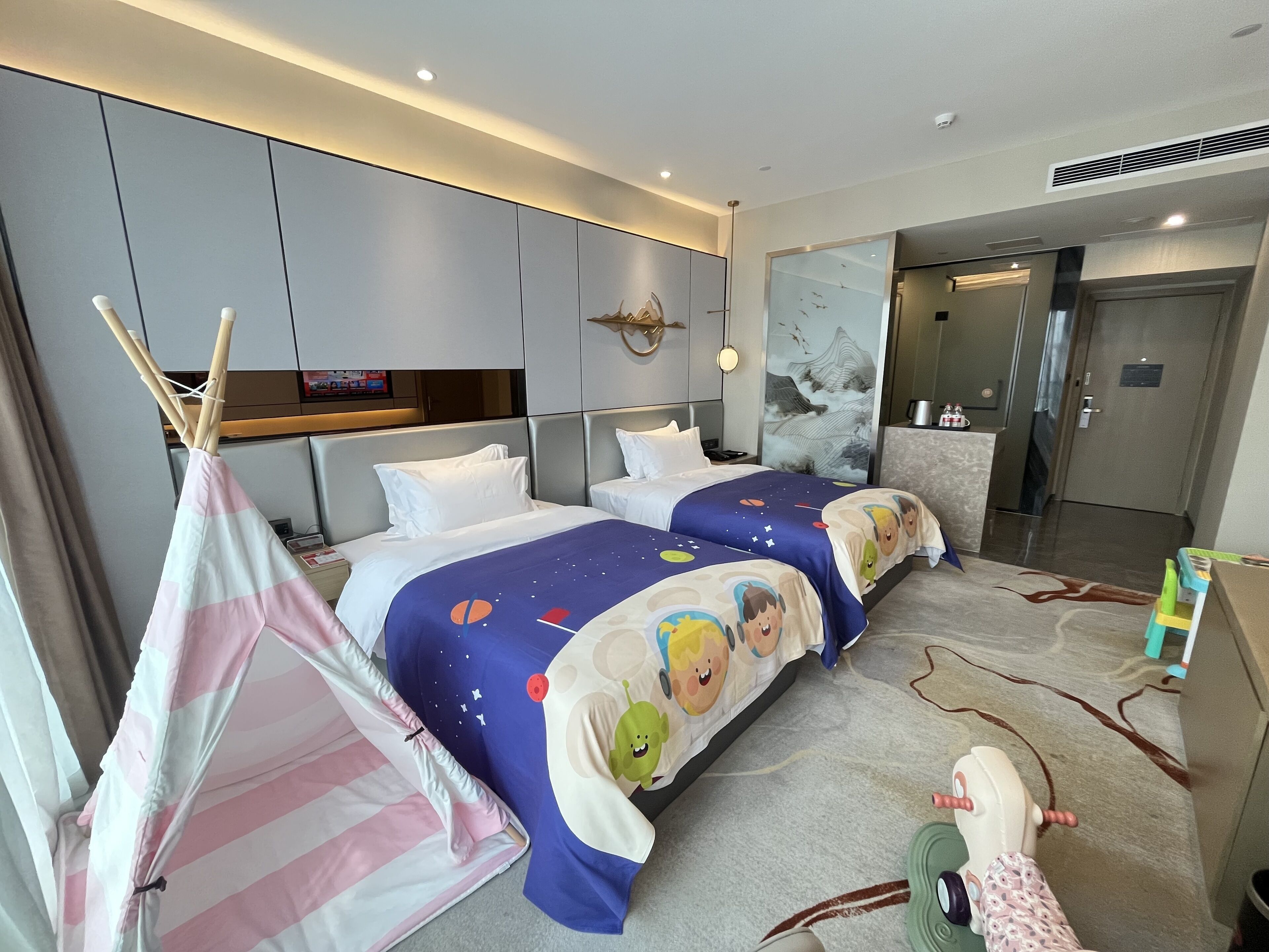Quarto de hotel com duas camas, uma televisão, um quadro e uma estrutura semelhante a uma tenda.
