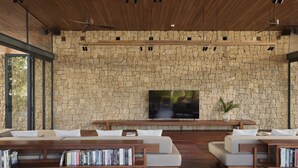 Uma sala de estar moderna com parede de pedra, uma televisão de tela plana e dois sofás com uma mesinha de centro à frente.
