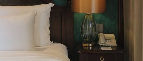 Quarto de hotel com uma cama, mesa de cabeceira com abajur e um quadro na parede.