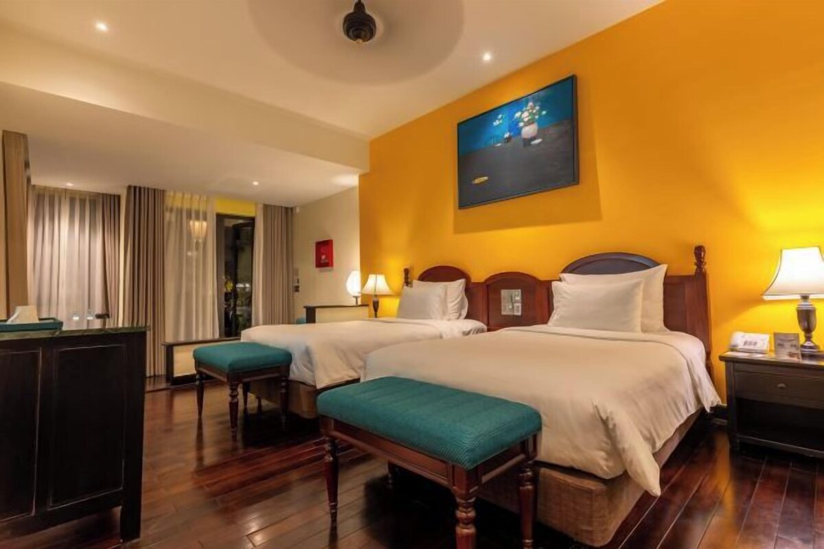 Quarto de hotel com duas camas, uma escrivaninha e um quadro na parede.