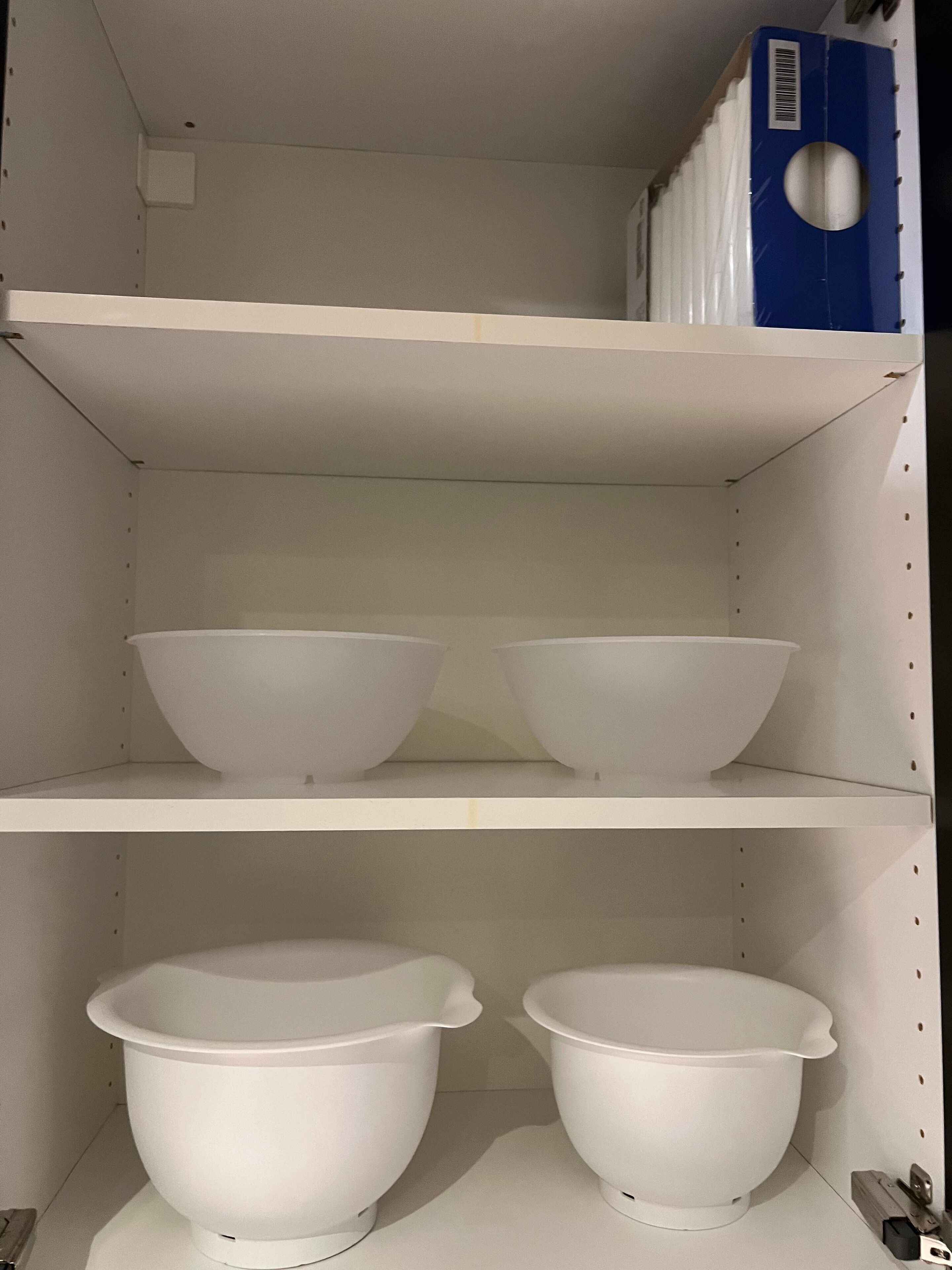 Cozinha com armários brancos e duas tigelas brancas na prateleira inferior.