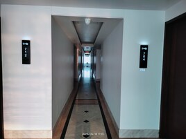 Um corredor de hotel moderno com janelas do chão ao teto, uma luminária central e os números de acesso aos elevadores 712 e 704.