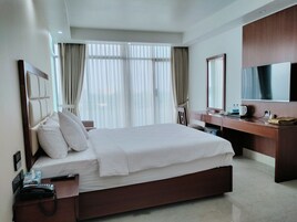 Quarto de hotel com uma cama grande, uma escrivaninha com telefone, um espelho e uma televisão.