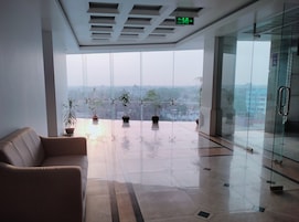 Um lobby moderno com parede de vidro, plantas em vasos, um sofá e teto com iluminação embutida.