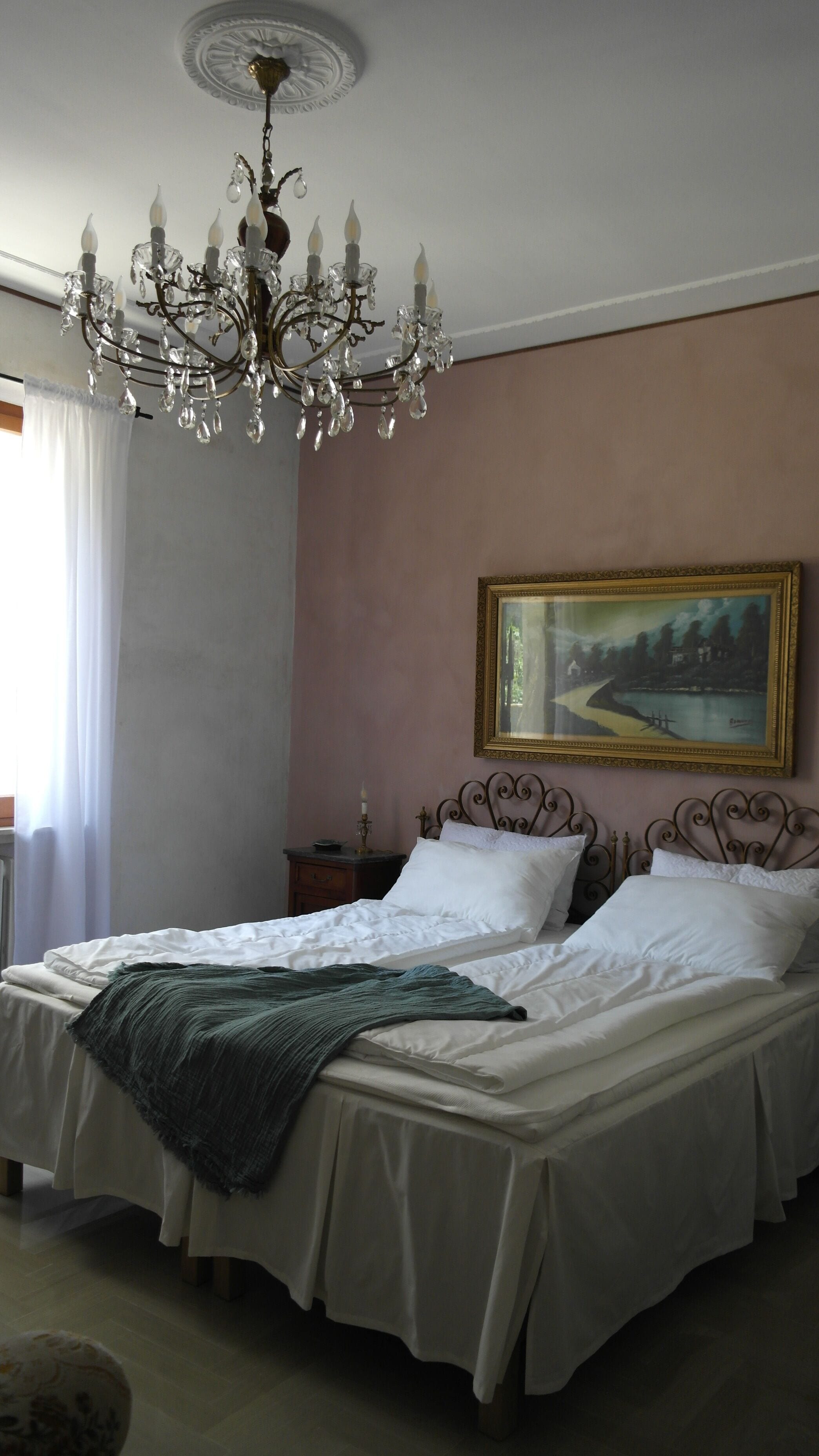 Quarto com duas camas, um candelabro, um quadro na parede e uma janela com cortinas.