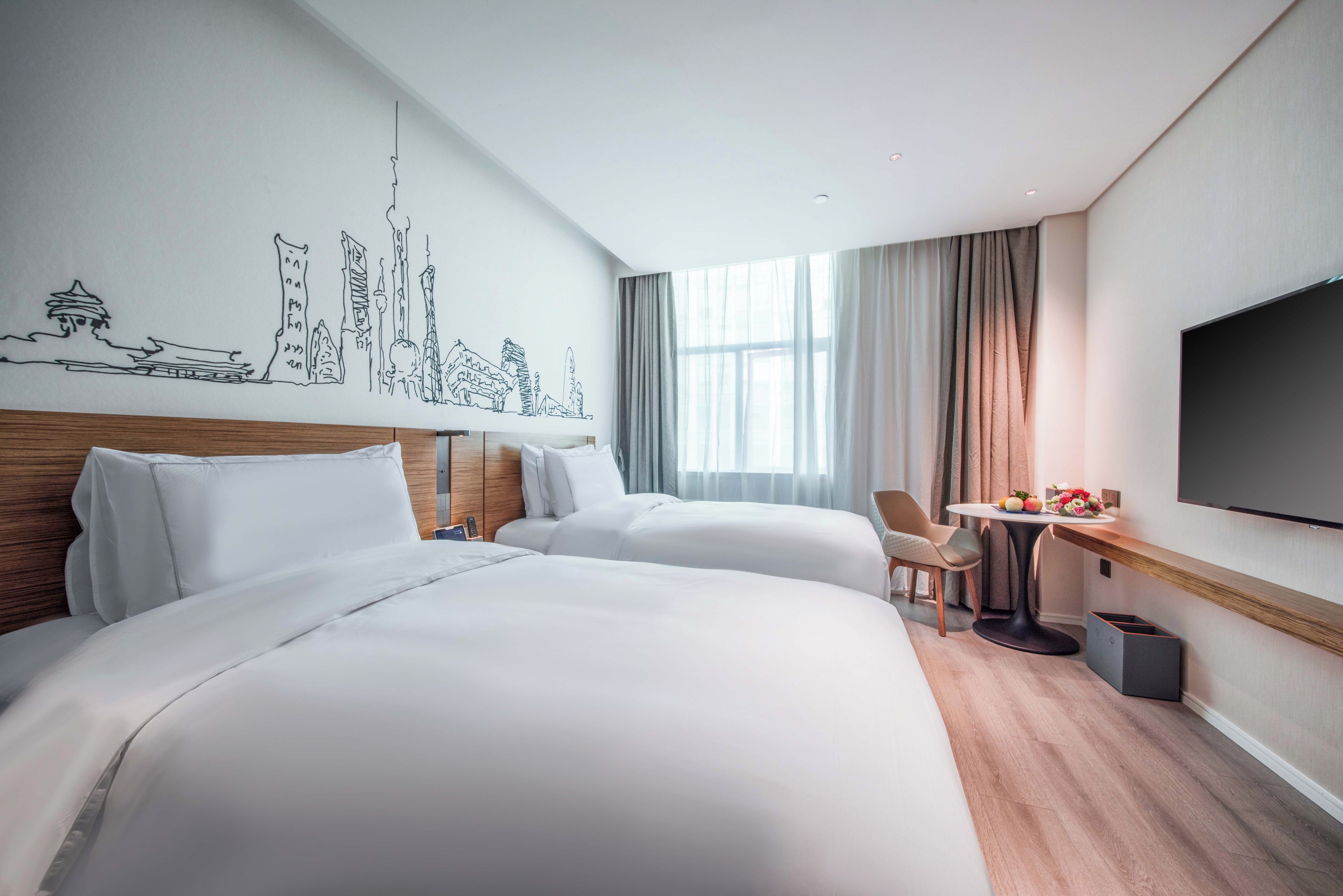 Quarto de hotel com duas camas, um mural da paisagem urbana, uma escrivaninha com cadeira, televisão e janela com cortinas.