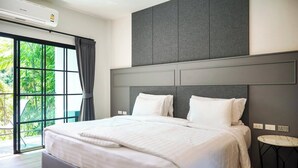Quarto moderno com uma cama grande, cabeceira cinzenta e uma pequena mesa redonda.