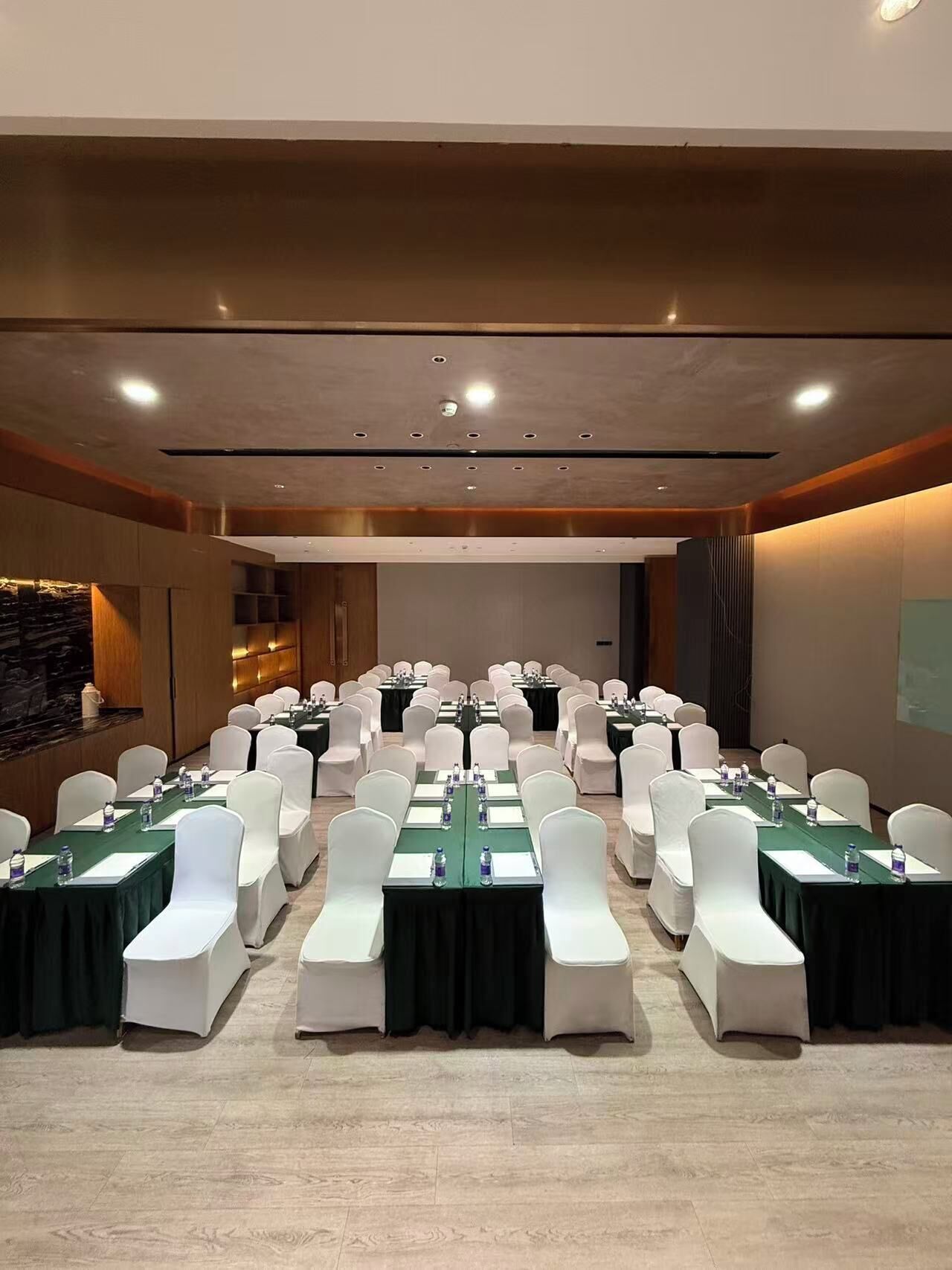 Sala de conferência com várias mesas e cadeiras, equipada com garrafas de água e placas de identificação.