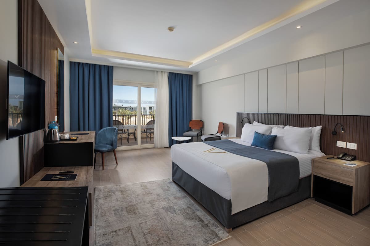 Quarto de hotel moderno com uma cama grande, uma escrivaninha, televisão e varanda com vista.