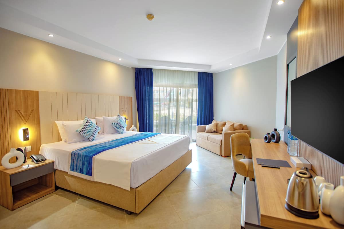 Quarto de hotel moderno com uma cama grande, uma escrivaninha com cadeira, uma televisão de tela plana e uma cafeteira.